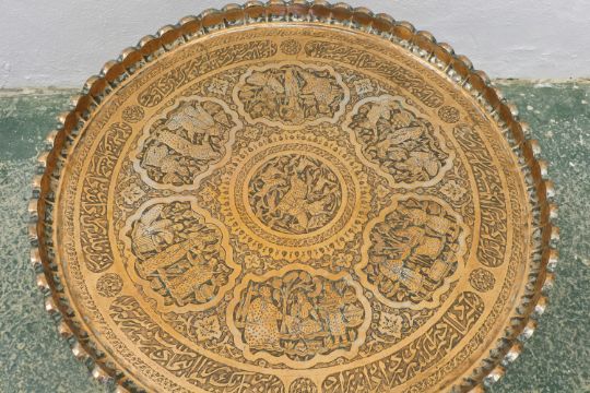 A circular Persian copper tray/table, decorated with scenes within ...