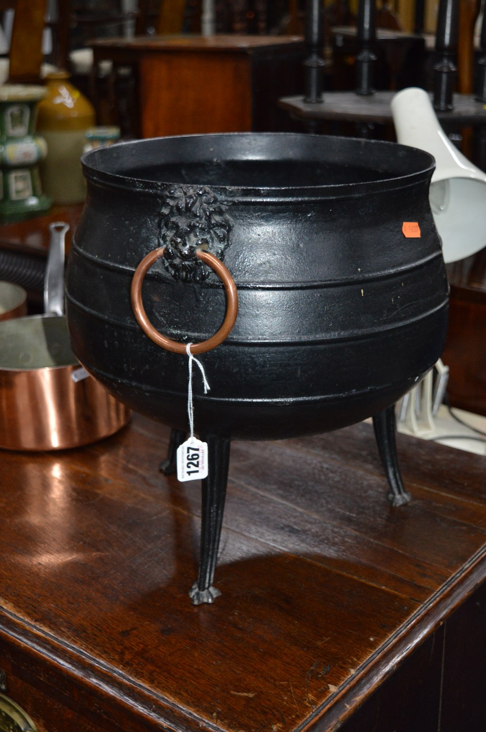 A CAST IRON CAULDRON, with brass circular handles on raised tripple ...