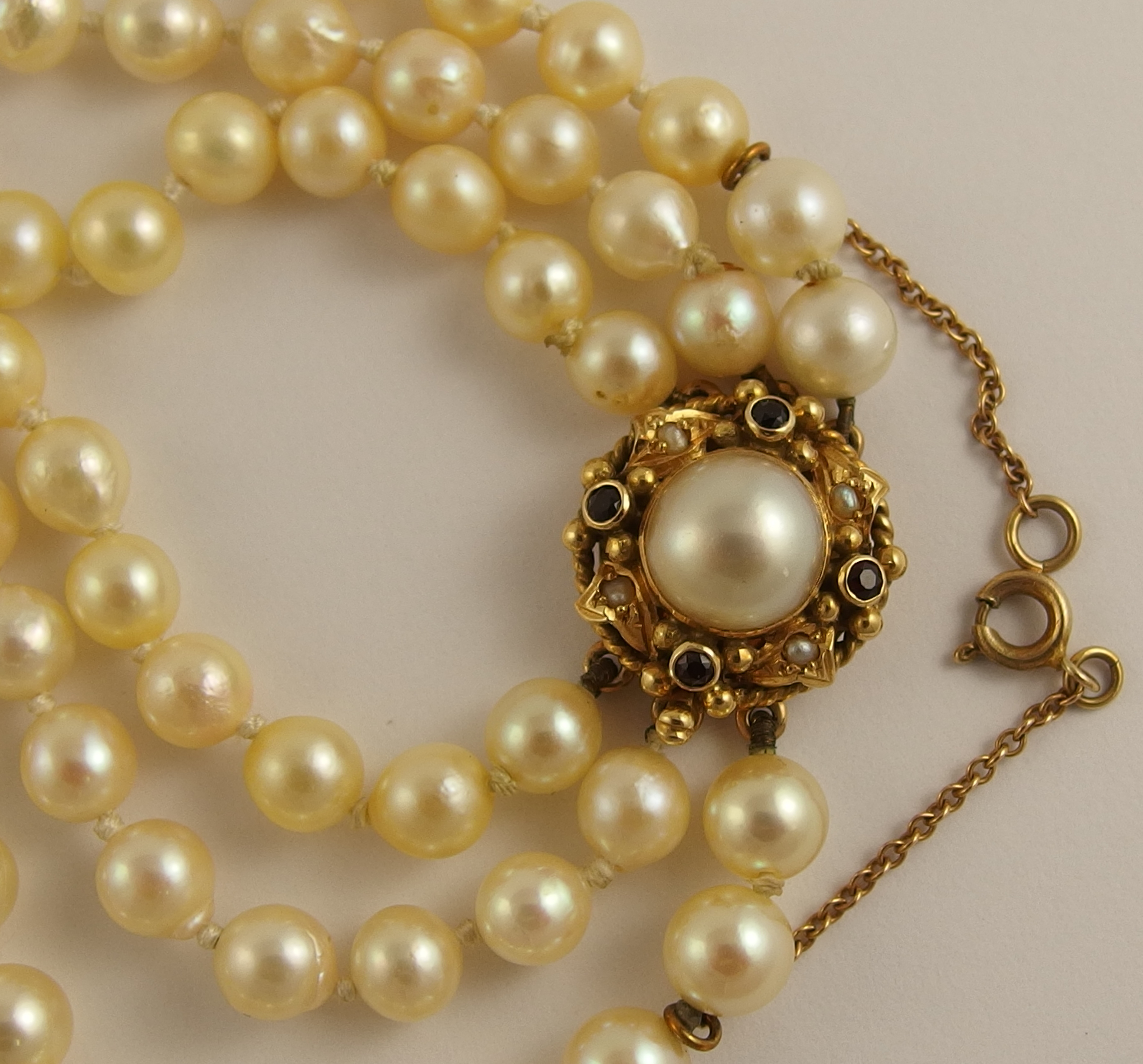 A triple string of pearls with a garnet and pearl clasp the gold ...