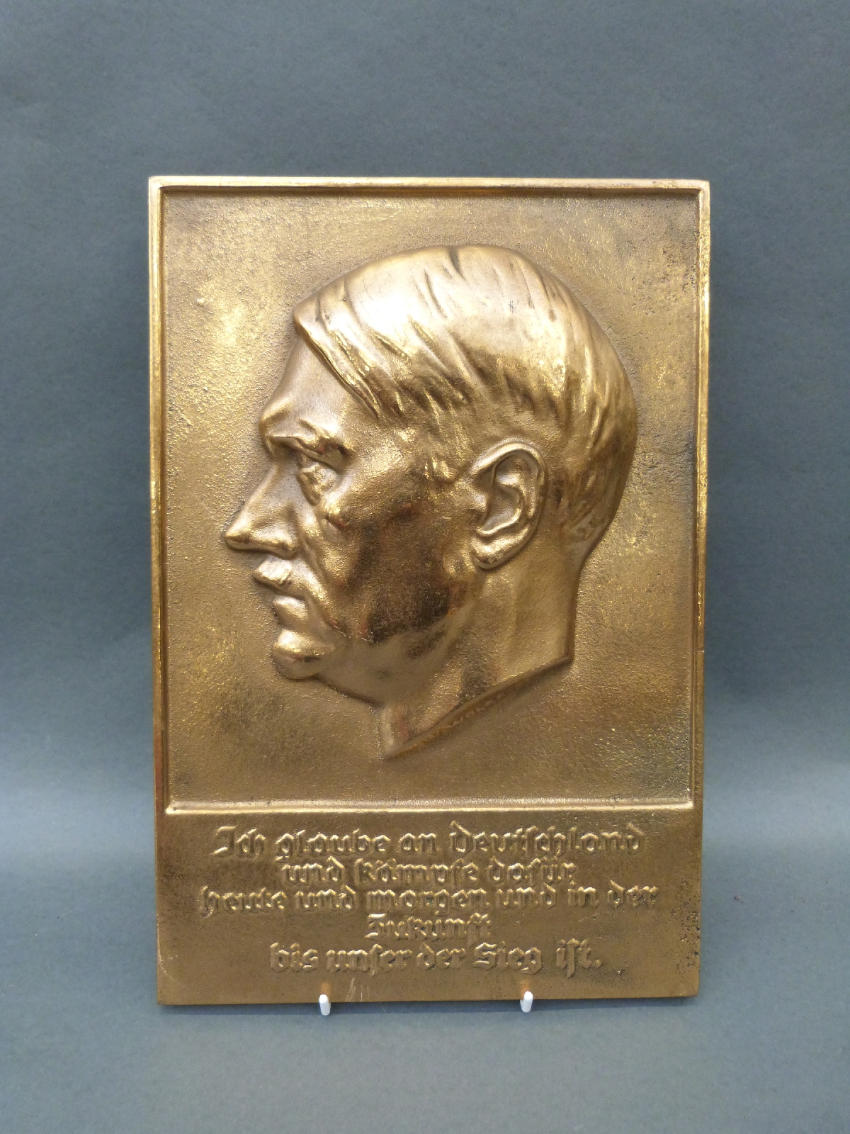 A German brass or bronze plaque of Adolf Hitler with motto below, 32 x 21cm