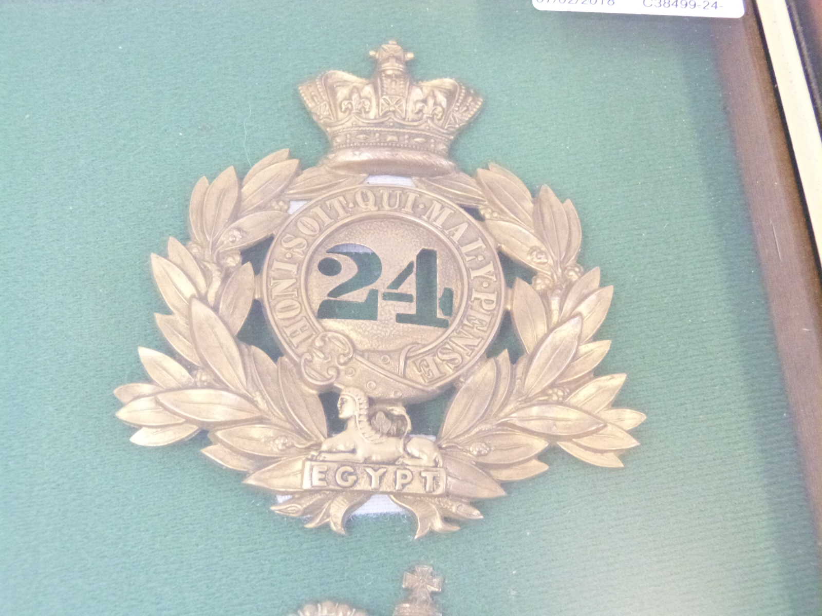 A framed collection of badges and helmet plates to the 24th Regiment of ...